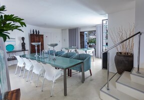 Uma sala de jantar moderna com mesa de vidro e cadeiras listradas, uma escada com corrimão e vista para o exterior.