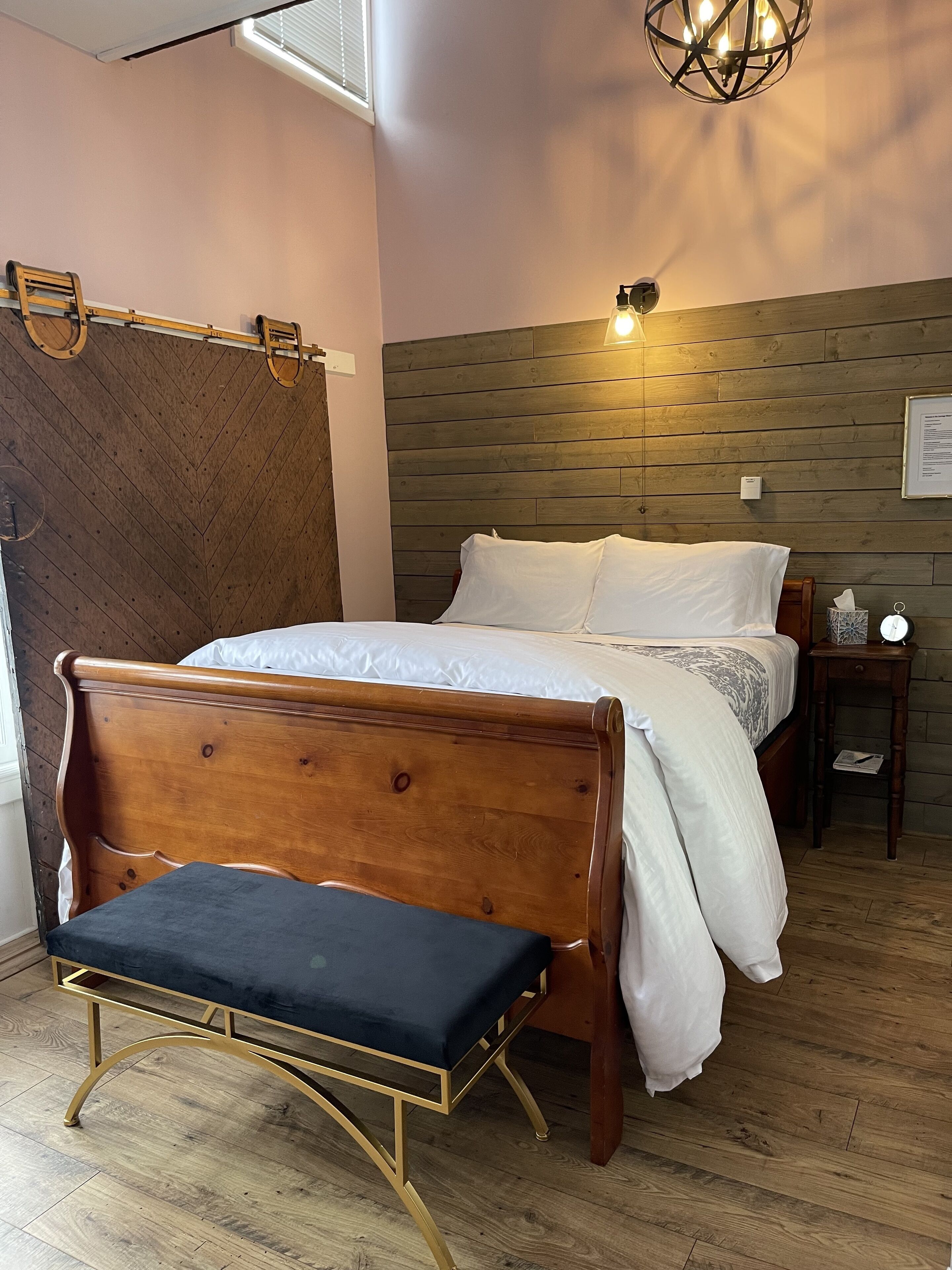 Quarto bem arrumado com cabeceira de madeira, mesa de cabeceira com abajur e um banco aos pés da cama.