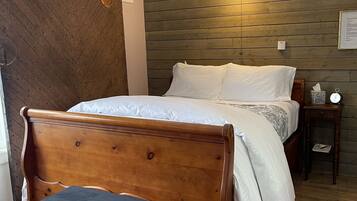 Quarto bem arrumado com cabeceira de madeira, mesa de cabeceira com abajur e um banco aos pés da cama.