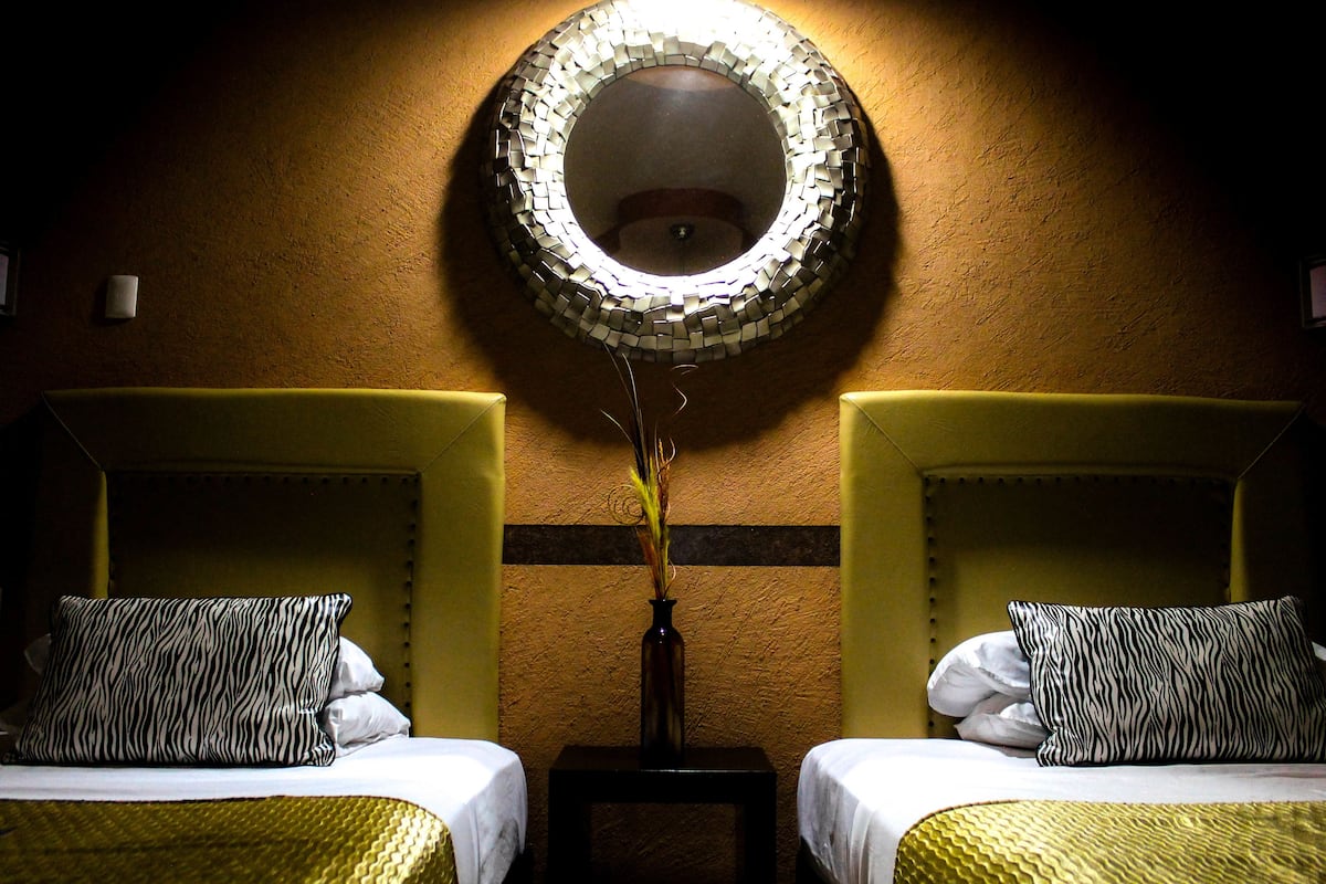 Quarto de hotel com duas camas, um espelho redondo na parede e um vaso com uma planta.
