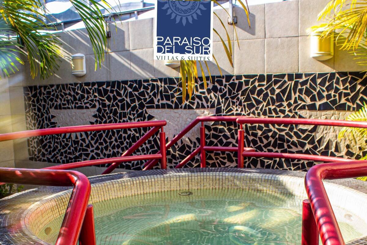 Uma banheira de hidromassagem com grades vermelhas, cercada por azulejos de mosaico e uma placa com o nome 'Paraiso del Sur Villas & Suites'.