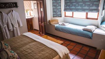Quarto com cama, janela com vista, mesa de cabeceira e prateleira na parede com toalhas.