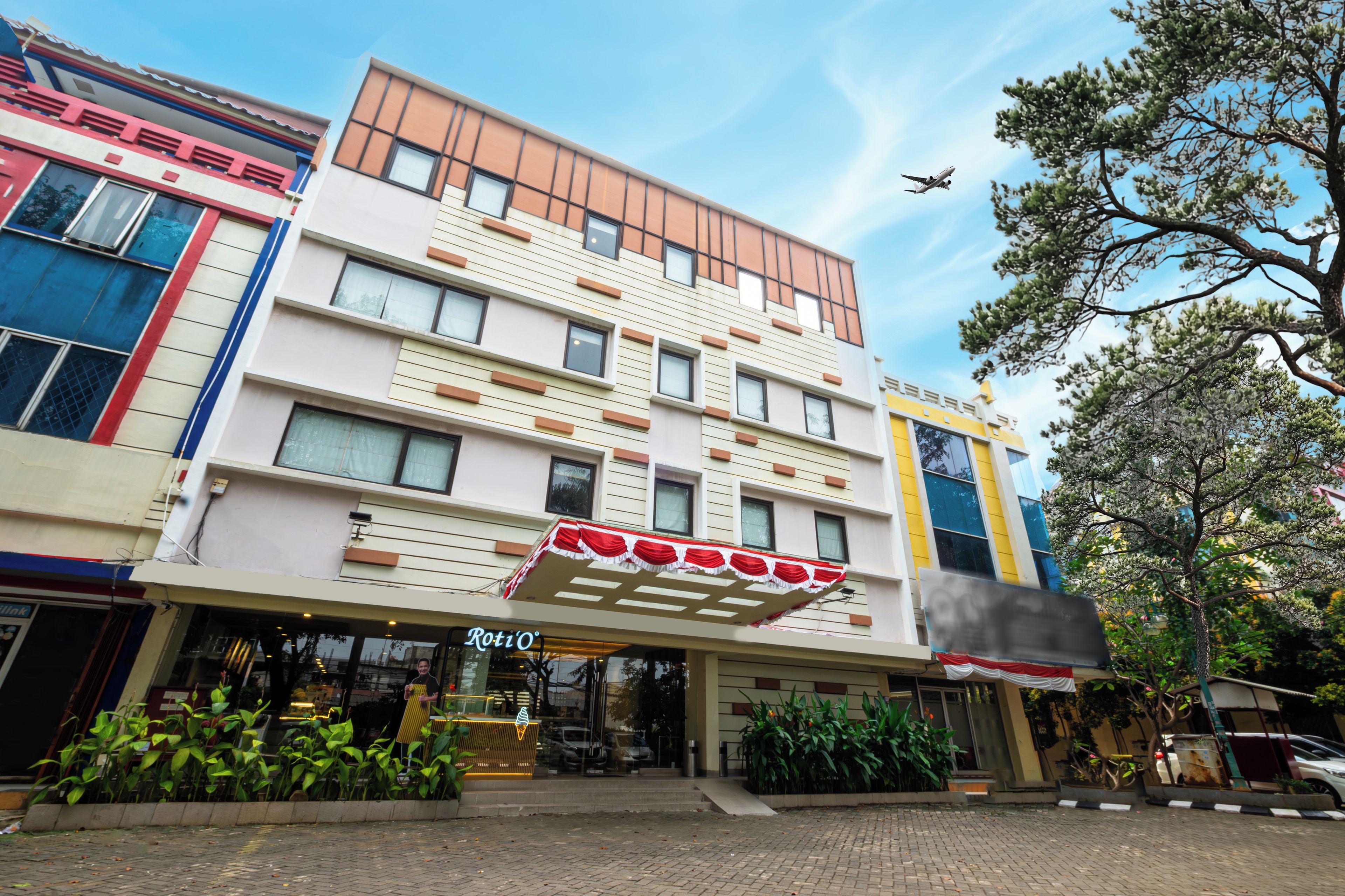 Um hotel com vários andares, restaurante no térreo e um avião visível no céu.