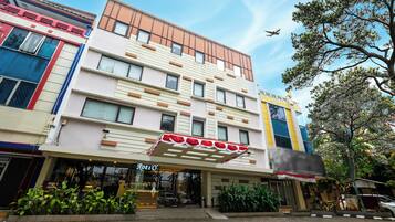 Um hotel com vários andares, restaurante no térreo e um avião visível no céu.
