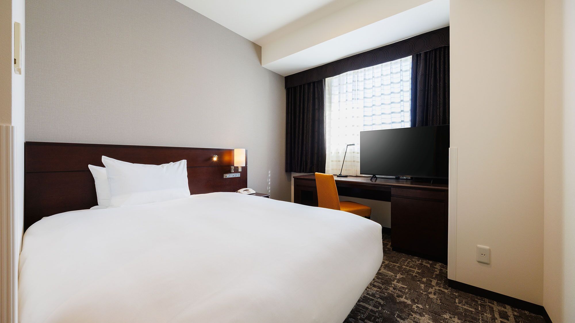 Quarto de hotel com uma cama grande, uma escrivaninha com cadeira, televisão e janela com cortinas.