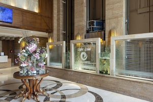 Um saguão com balcão de recepção, uma mesa decorativa com vasos e uma placa indicando o Fira Hotel.