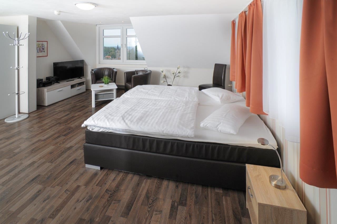Quarto moderno com uma cama grande, televisão, escrivaninha e cadeira.