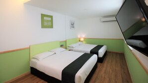 Quarto de hotel com duas camas, paredes verdes, televisão de tela plana e cartazes motivacionais.