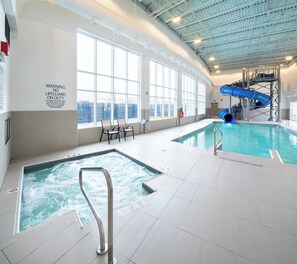 Piscina interna com banheira de hidromassagem, um escorregador de água azul e um aviso de salva-vidas.
