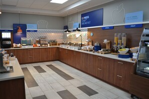 Uma sala de café da manhã moderna, com balcão, diversas estações de comida e uma máquina de café.