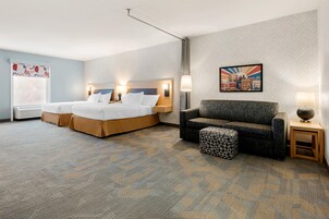 Quarto de hotel com cama, sofá, carpete estampado e pintura de paisagem urbana na parede.