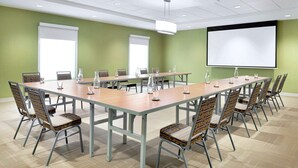 Uma sala de conferência com uma mesa comprida, cadeiras, tela de projetor e um janelão.