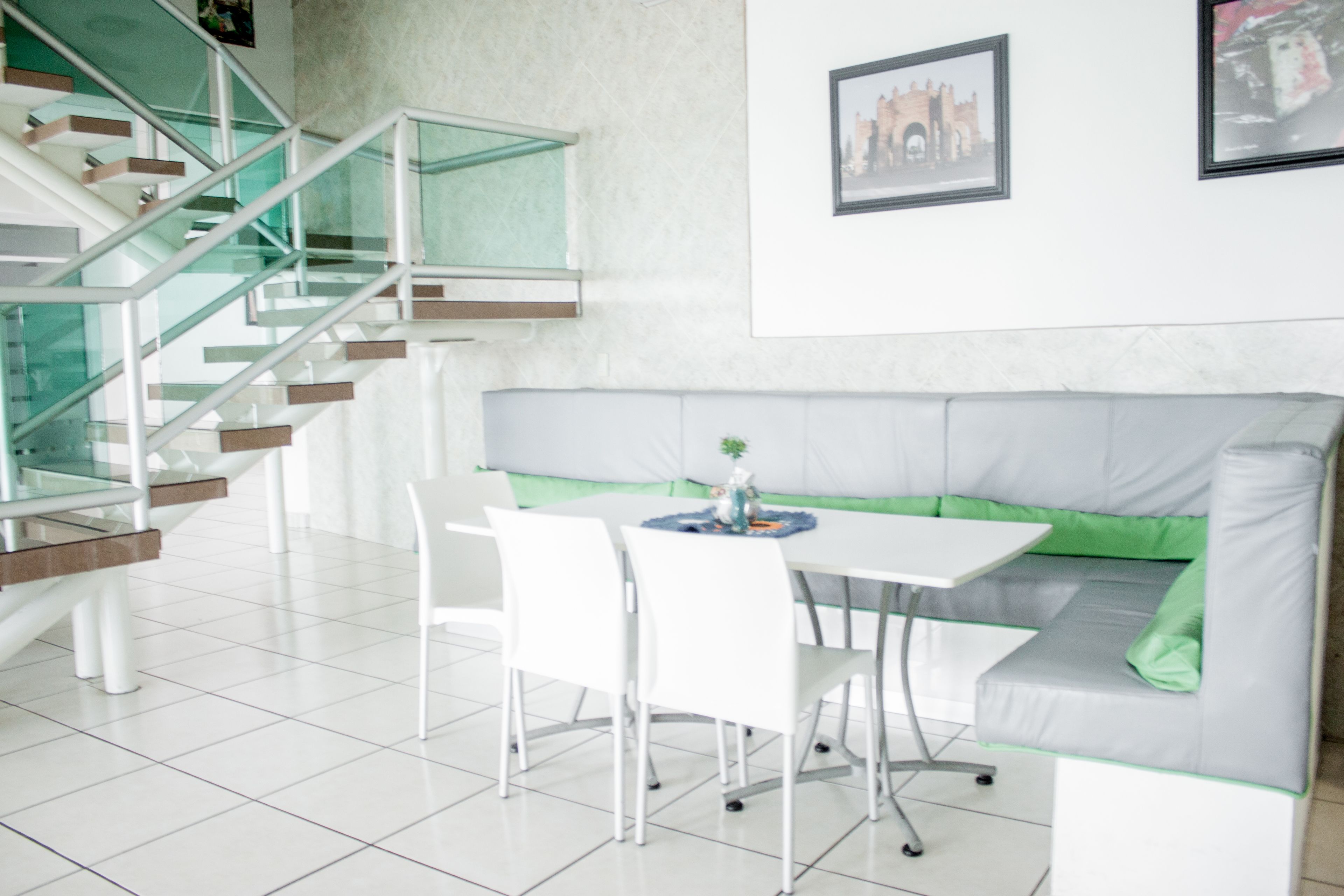 Um interior moderno com escada, área de refeições em branco e um sofá cinza com almofadas verdes.