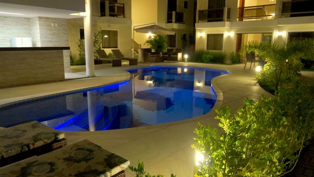 Piscina com design sinuoso, rodeada por espreguiçadeiras e plantas em vasos.