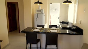 Uma cozinha compacta com micro-ondas, pia e área de refeições com duas cadeiras e uma mesa posta para dois.