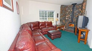 Uma sala de estar com um amplo sofá de couro, uma parede de pedra, uma lareira e uma televisão sobre um suporte de madeira.