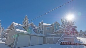 Uma casa de dois andares com garagem, rodeada por árvores cobertas de neve.