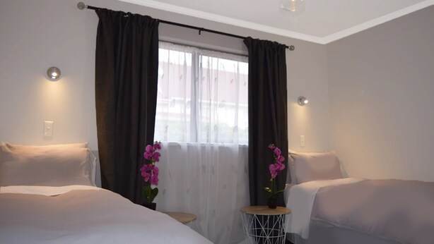 Quarto de hotel com duas camas, uma mesinha redonda e uma janela com cortinas.