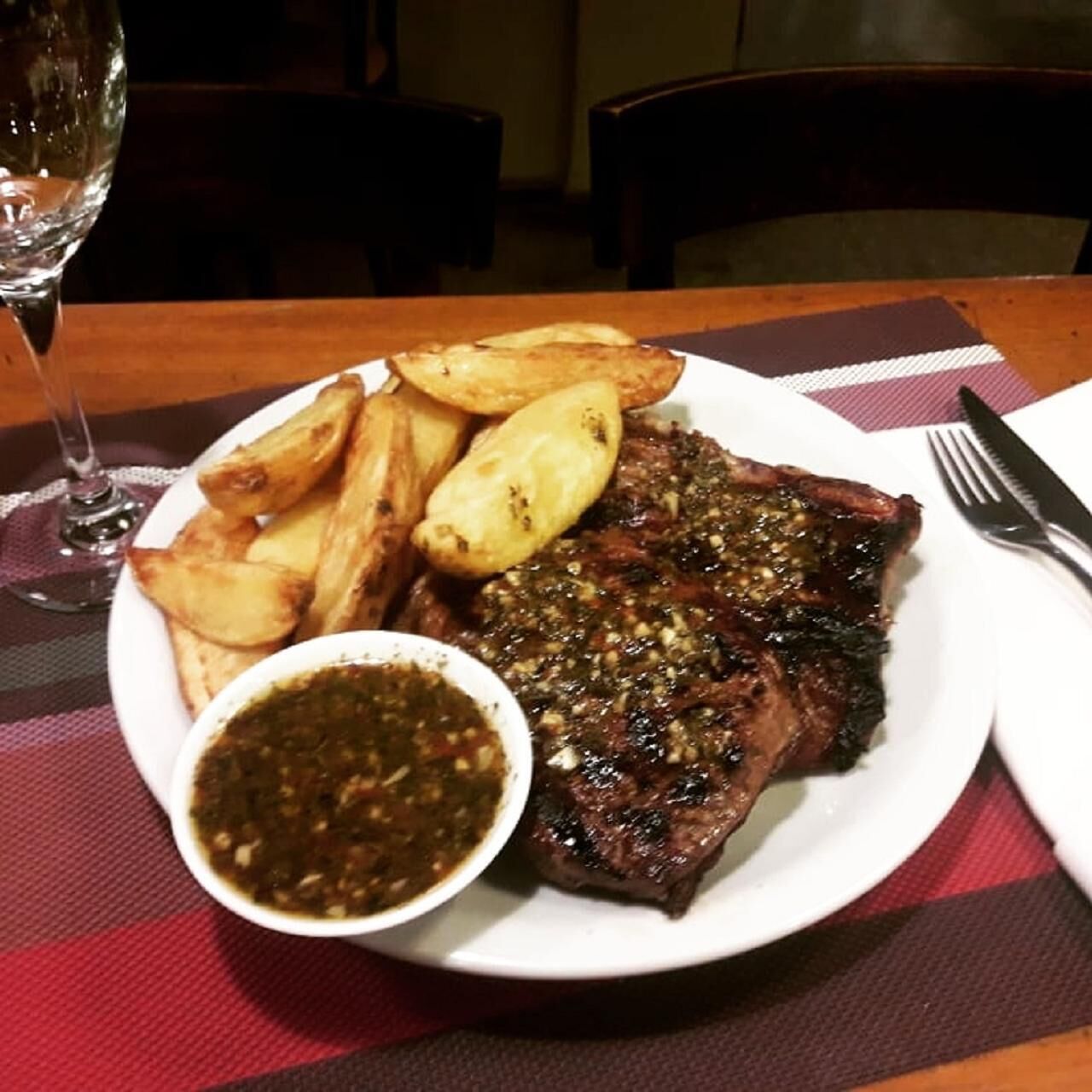 Um prato com bife, batatas assadas e acompanhamento de molho.