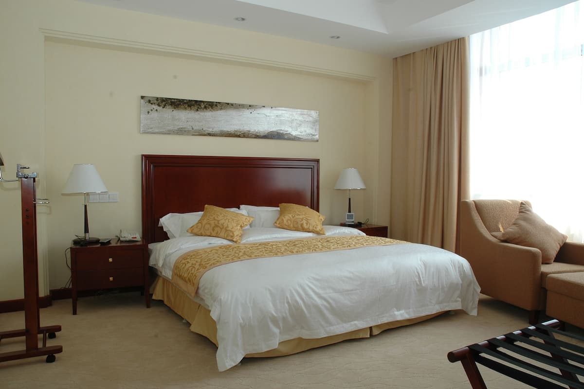 Quarto de hotel com uma cama grande, duas mesas de cabeceira, uma cadeira e uma janela com cortinas.