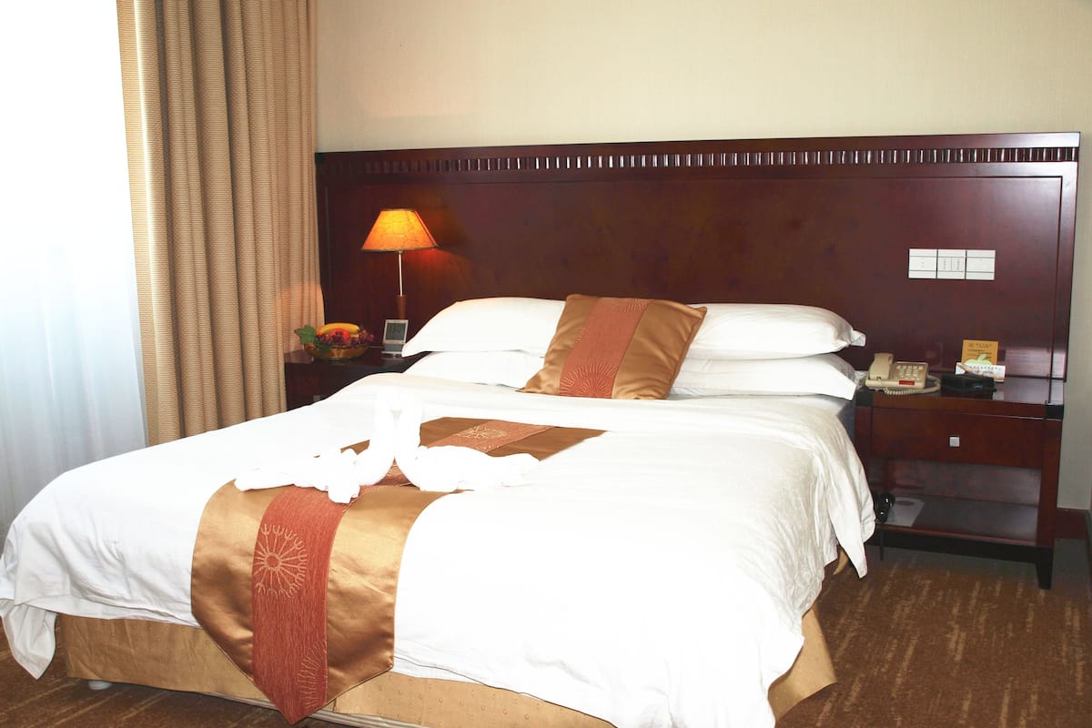 Quarto de hotel com uma cama bem arrumada, uma luminária de cabeceira, uma fruteira e um telefone no criado-mudo.