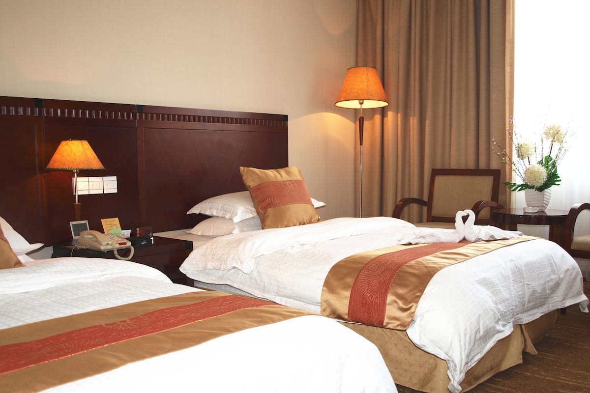 Quarto de hotel com duas camas, uma mesa de cabeceira com telefone e uma luminária.