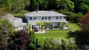 Uma casa grande de dois andares com varanda coberta e gramado bem cuidado.