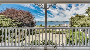 Varanda coberta com balaustrada branca, com vista para um jardim ajardinado e o mar.