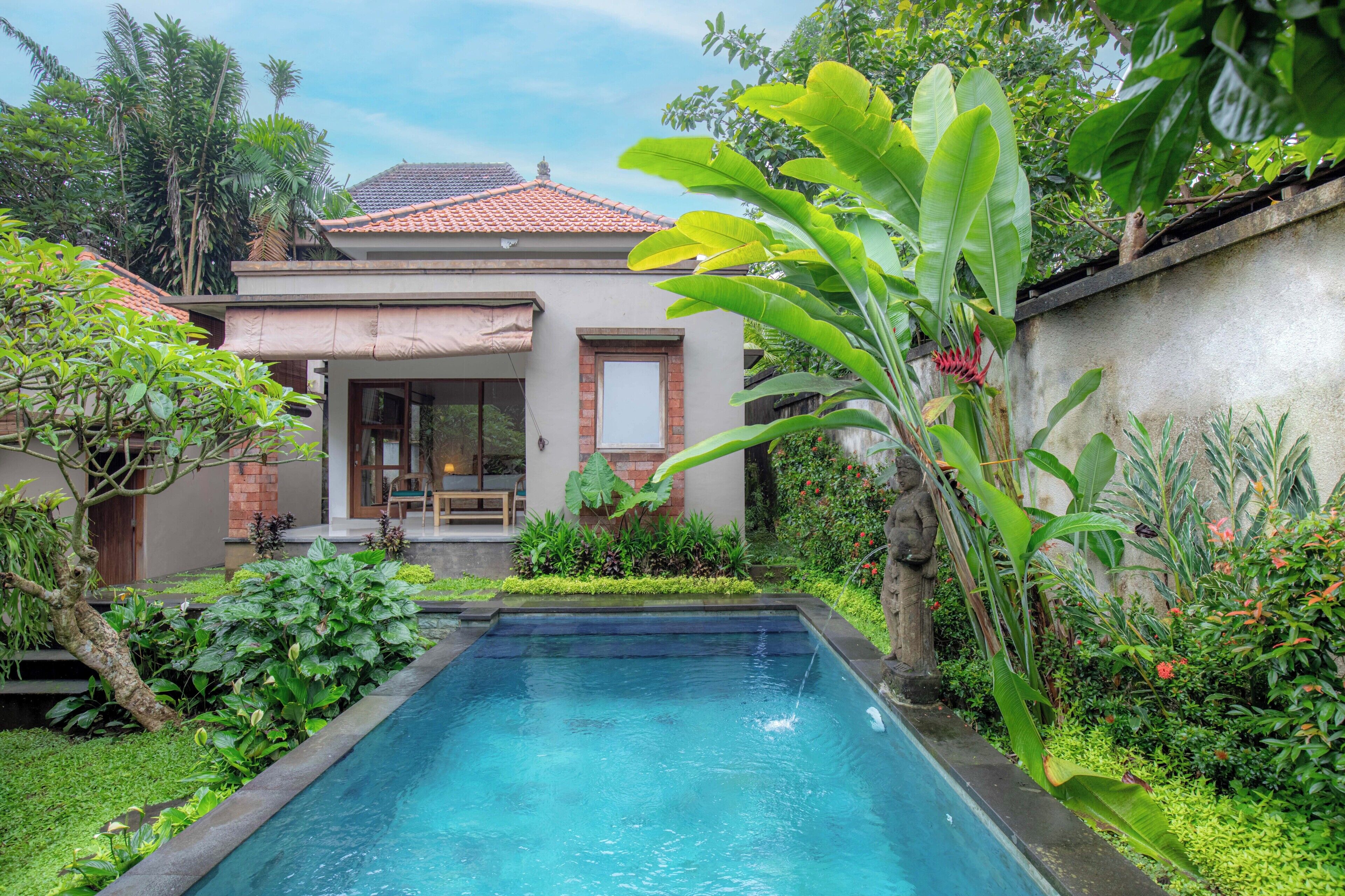 Piscina cercada por vegetação exuberante e uma casa com telhado de azulejos.