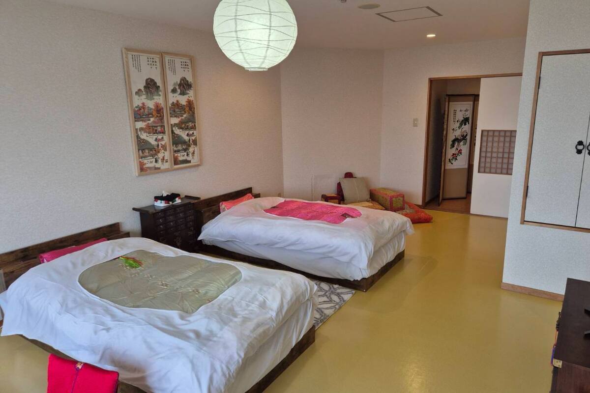 Quarto de hotel com duas camas, luminária suspensa em estilo tradicional japonês e obras de arte nas paredes.
