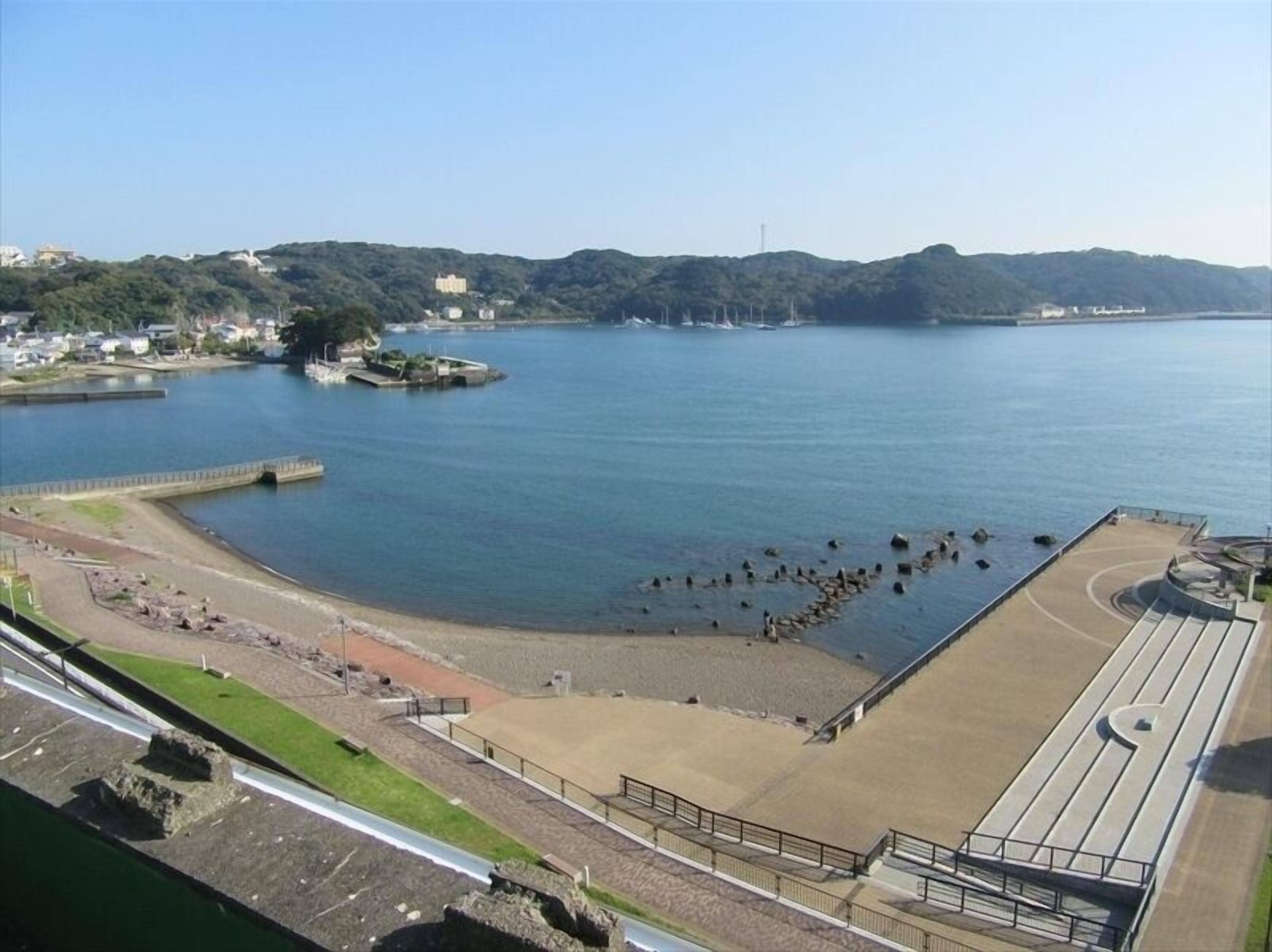 Uma área costeira com uma praia arenosa, um pequeno cais e um estádio.