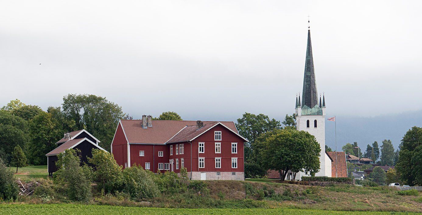 Um edifício vermelho com uma torre branca, rodeado por vegetação e árvores.