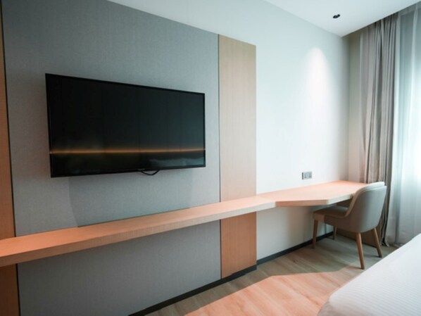 Quarto de hotel moderno com televisão de tela plana na parede, uma escrivaninha de madeira e uma cadeira.