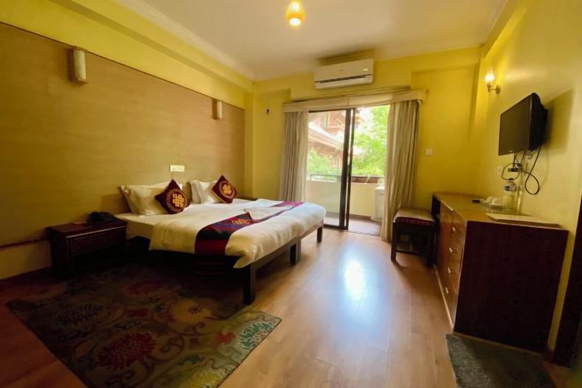 Quarto de hotel com cama, escrivaninha, televisão e varanda com cortinas.