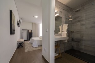 Uma casa de banho moderna com cabine de duche em vidro, lavatório branco e banco de madeira.