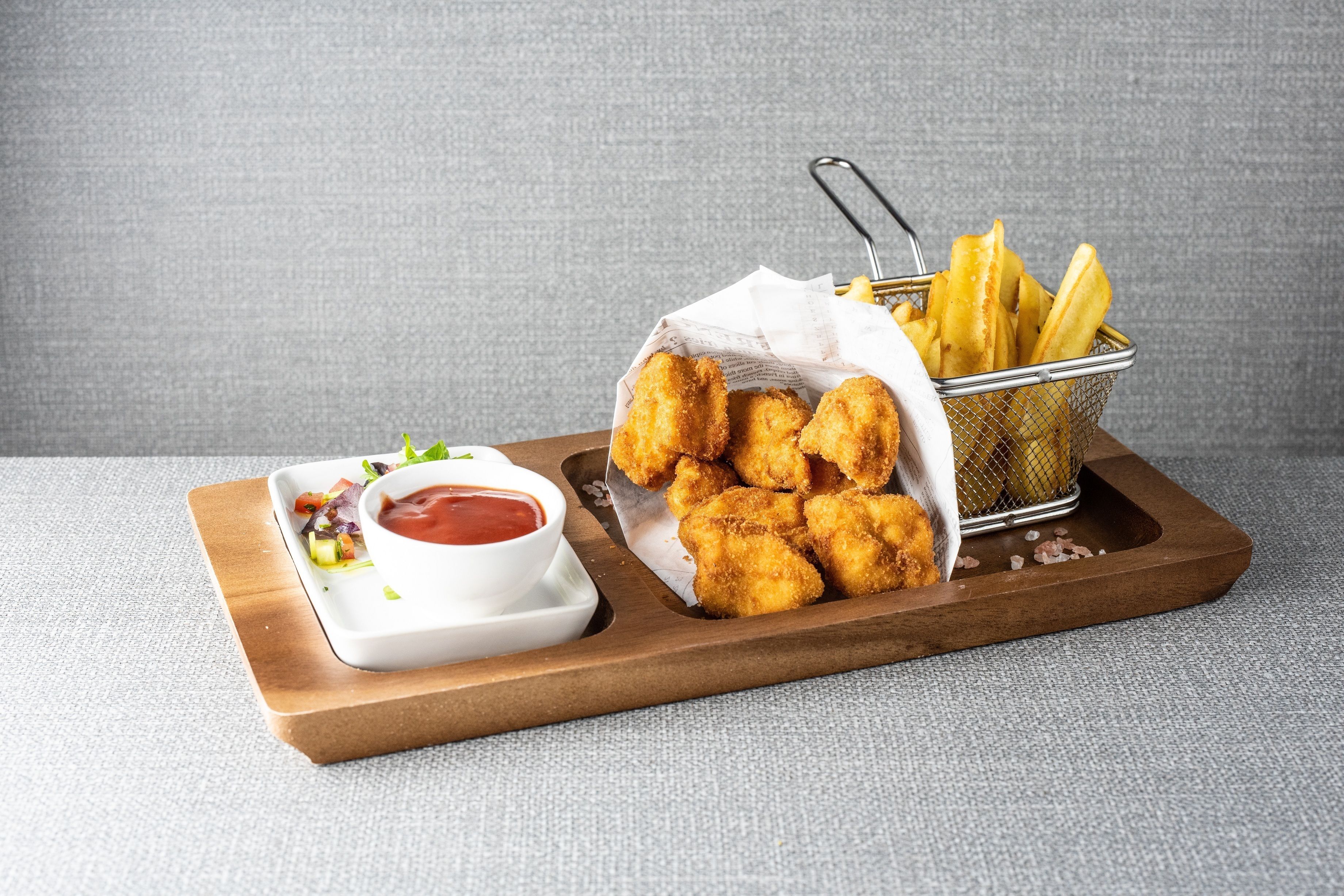 Uma bandeja com tiras de frango frito, um cesto de batatas fritas e uma pequena tigela de ketchup.