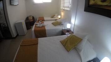 Quarto de hotel com duas camas, uma escrivaninha, uma cadeira, uma televisão e janela com persianas.
