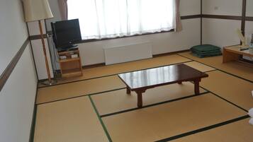 Quarto com piso de tatame, televisão em suporte, mesa e janela com cortinas.