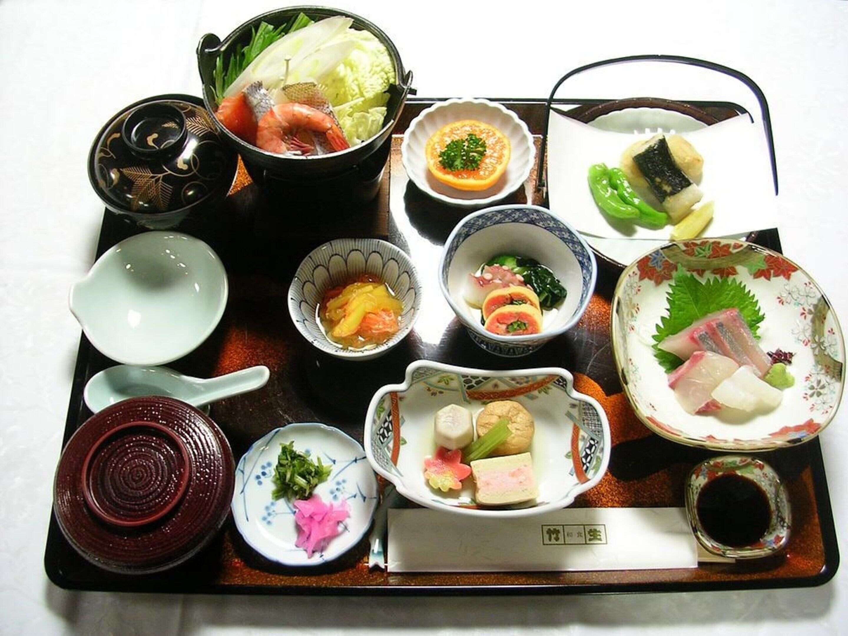 Uma bandeja tradicional japonesa com diversos pratos, incluindo sashimi, legumes e uma pequena tigela de itens em conserva.