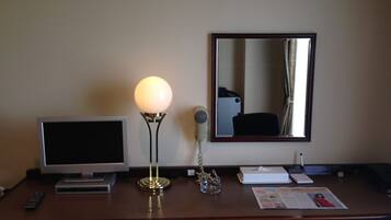 Mesa de quarto de hotel com televisão de tela plana, luminária, espelho e caixa de lenços.