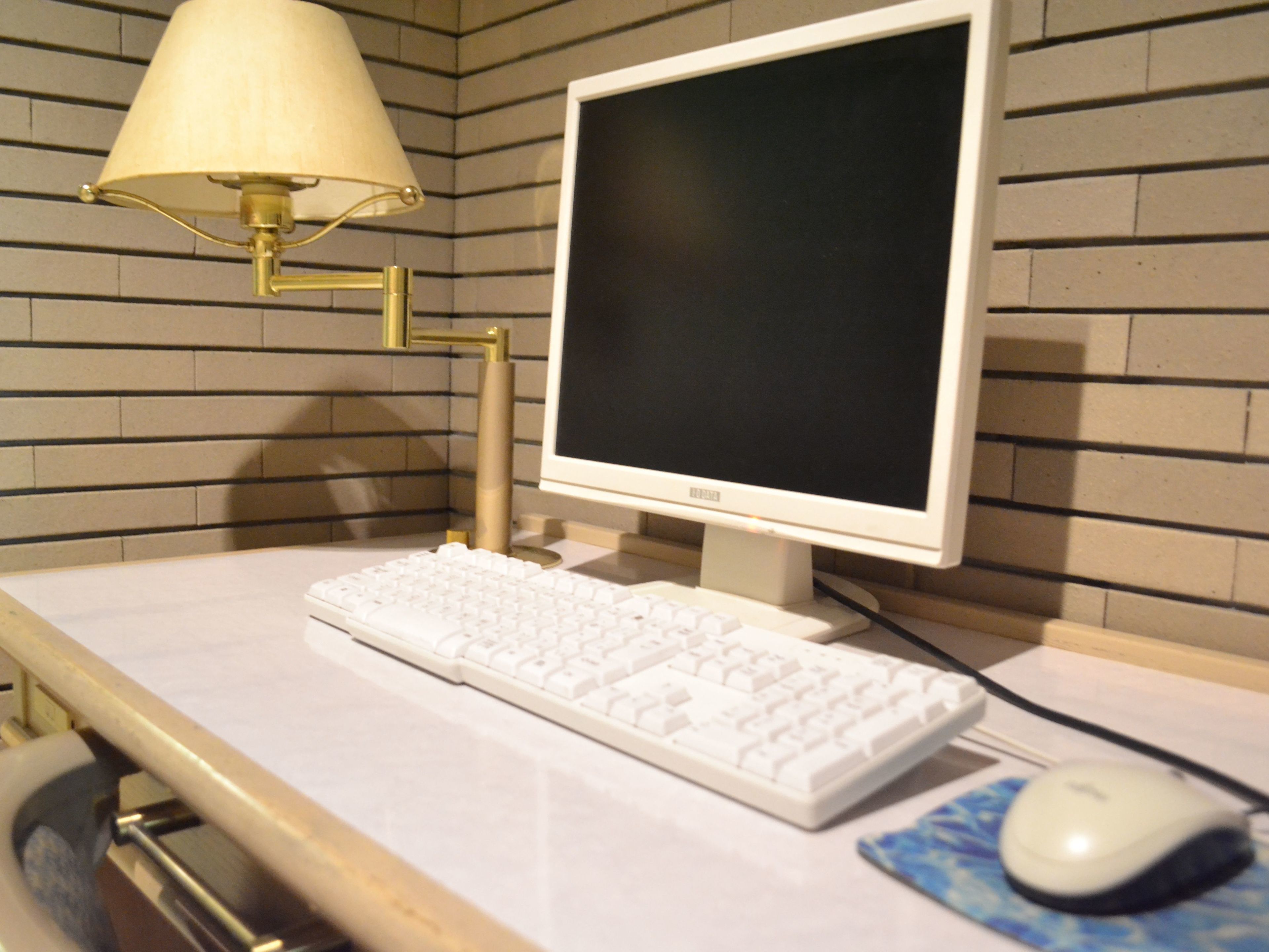 Uma mesa de computador com teclado branco, monitor e rato.