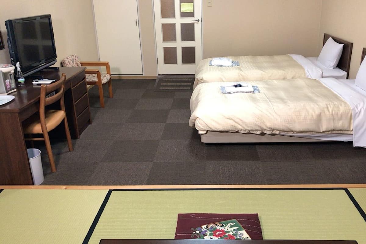 Quarto de hotel com duas camas, uma mesa de escritório com televisão, uma cadeira e uma mesinha.