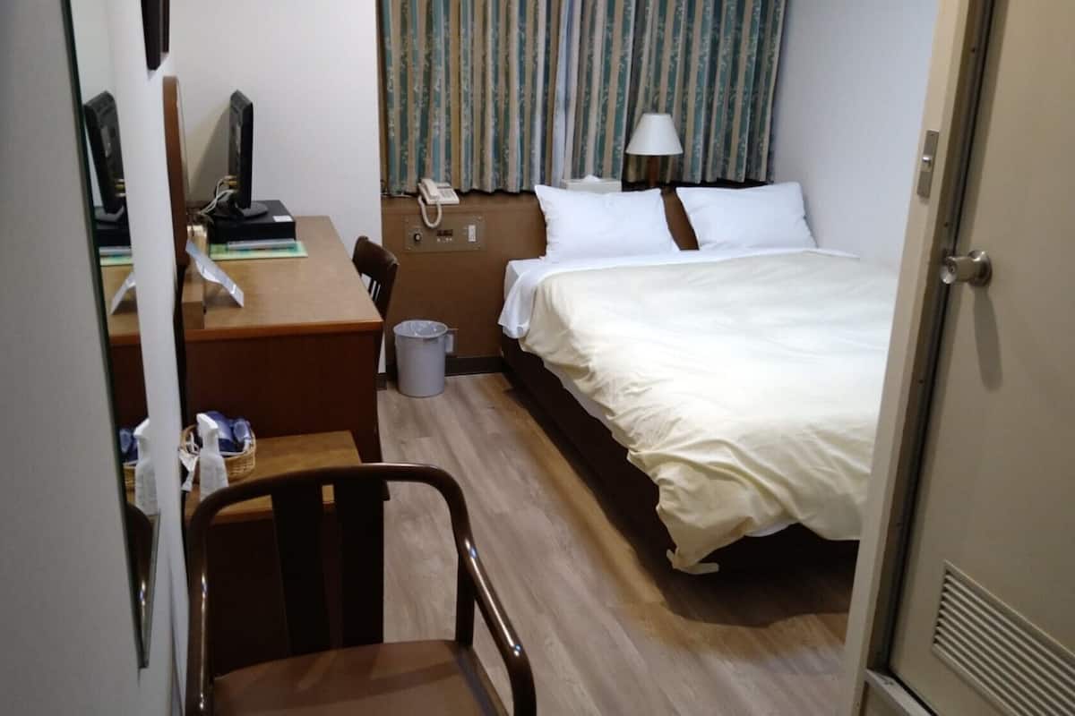 Quarto de hotel com cama, escrivaninha, cadeira e telefone.