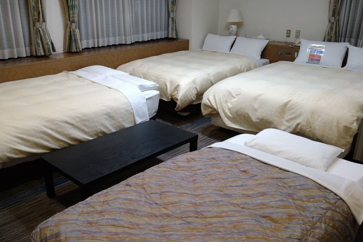 Quarto de hotel com duas camas, um banco e uma mesa de cabeceira com abajur.