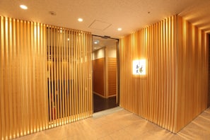 Um corredor com ripas verticais de madeira e uma placa iluminada com caracteres japoneses.