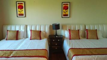 Quarto de hotel com duas camas, cada uma com roupa de cama branca e almofadas vermelhas e bege. Há quadros com rosas vermelhas na parede acima das camas.