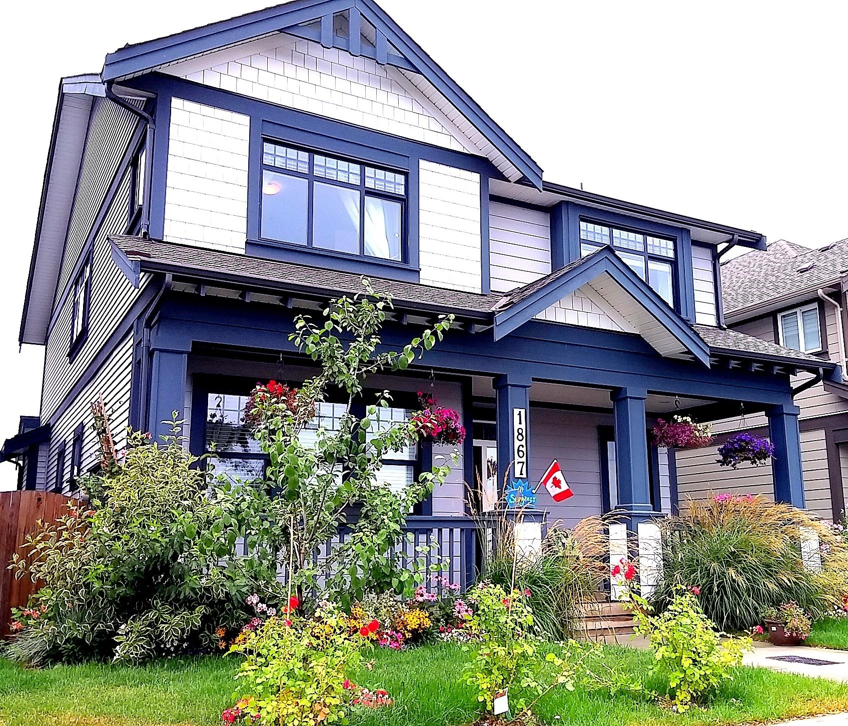 Uma casa de dois andares com varanda frontal, caixa de correio e a bandeira do Canadá.
