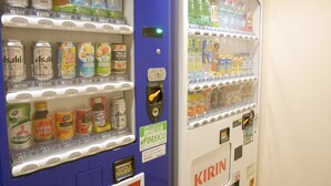 Máquina automática com diversas bebidas e lanches, incluindo latas e garrafas, com etiquetas de preço visíveis.