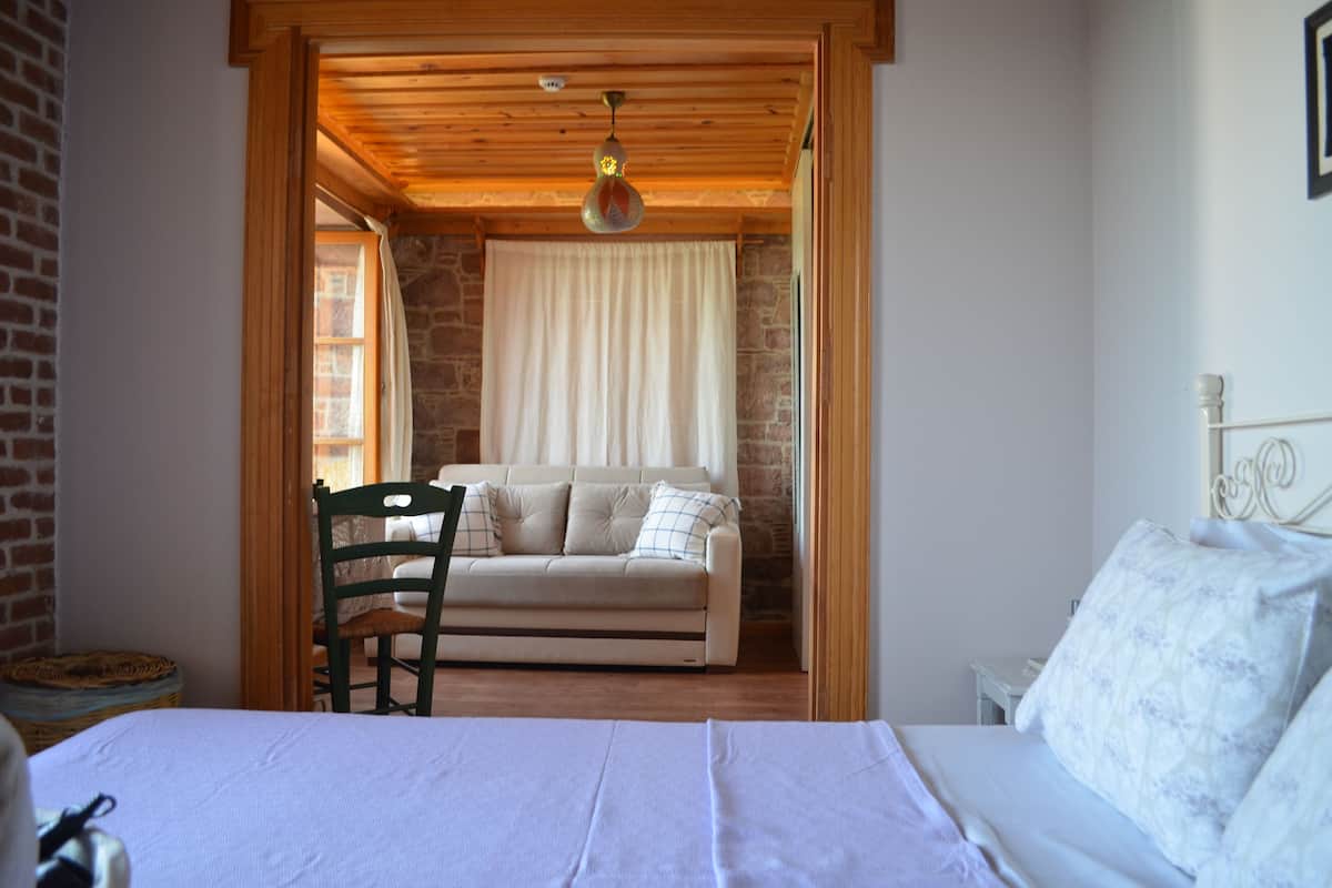 Quarto aconchegante com cama, poltrona, sofá e luminária pendente.