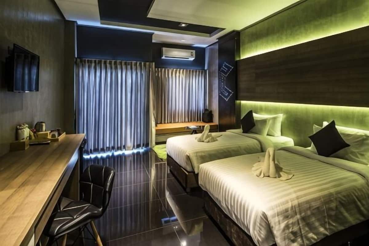 Quarto de hotel com escrivaninha, duas camas, televisão e janela com cortinas.